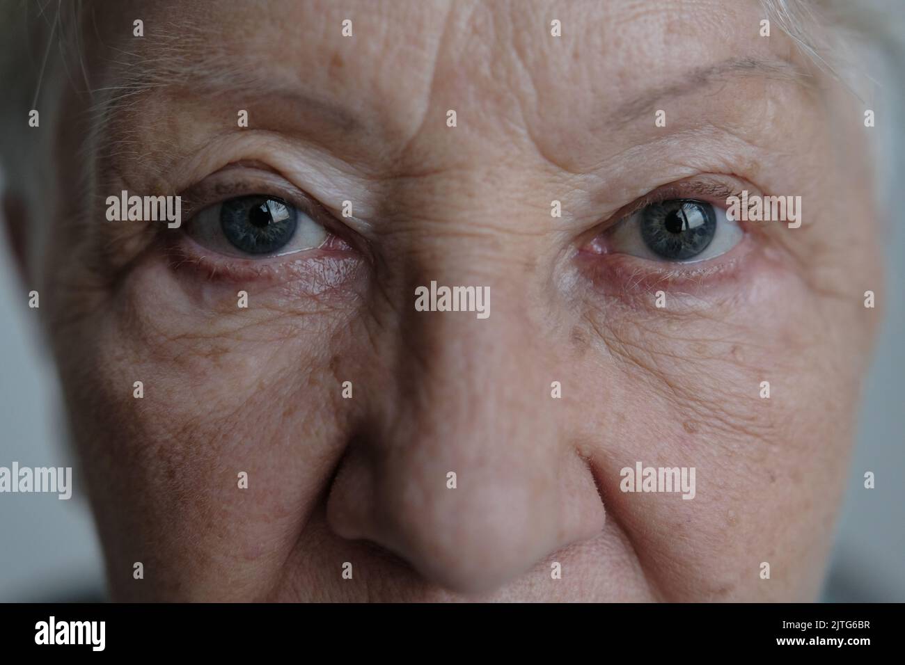 Close up portrait of beautiful older woman smiling and standing by wall with gray eyes Stock ...