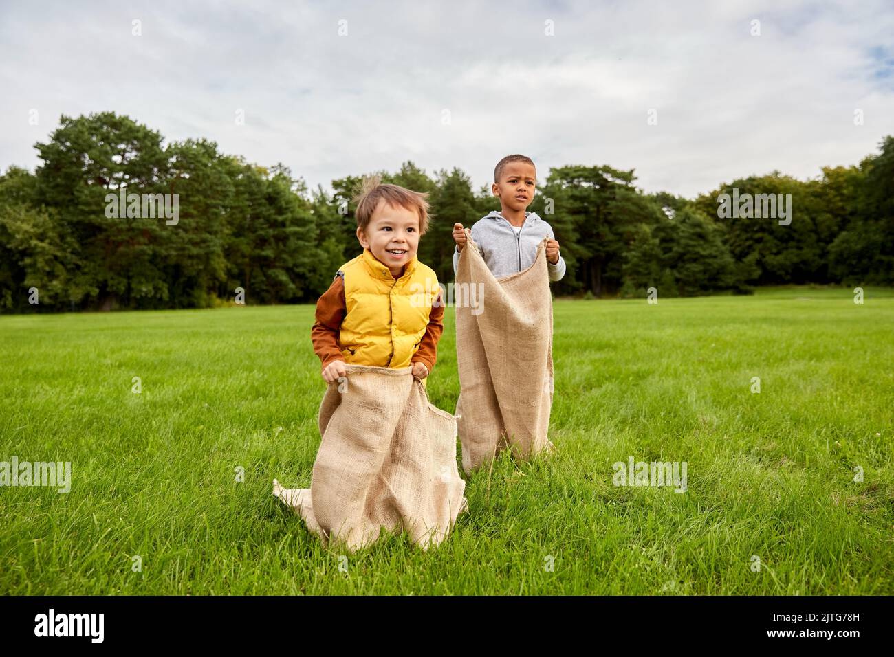 happy boys playing bag jumping game at park Stock Photo - Alamy