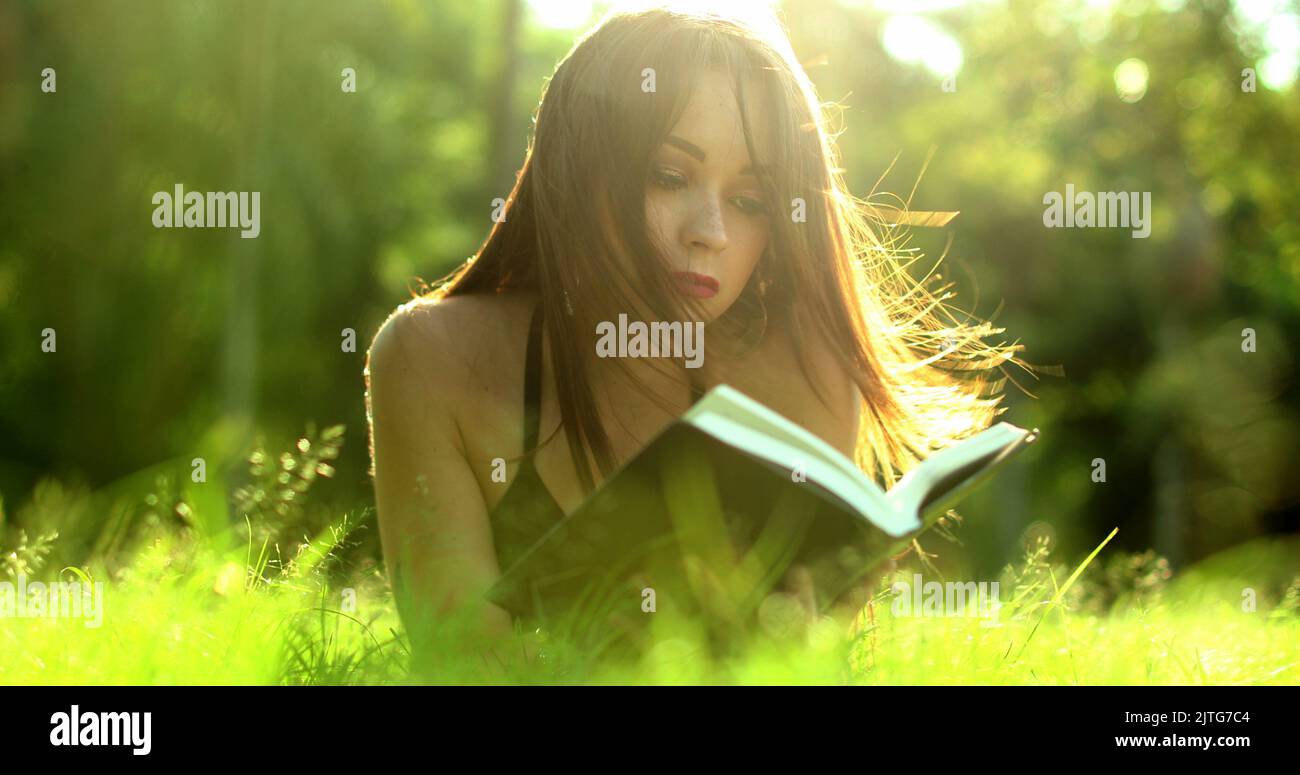 Woman reading book lying in grass at park. Pretty girl enjoying story ...