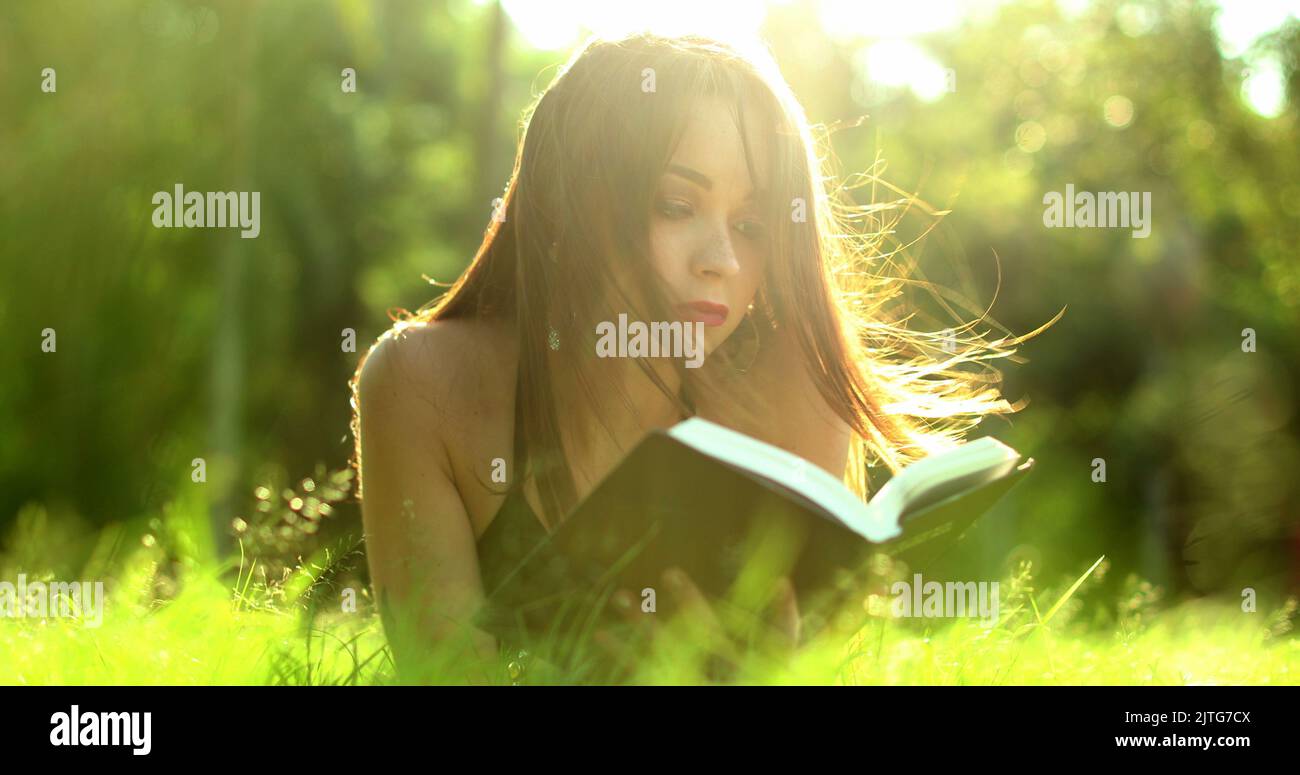 Woman reading book lying in grass at park. Pretty girl enjoying story ...