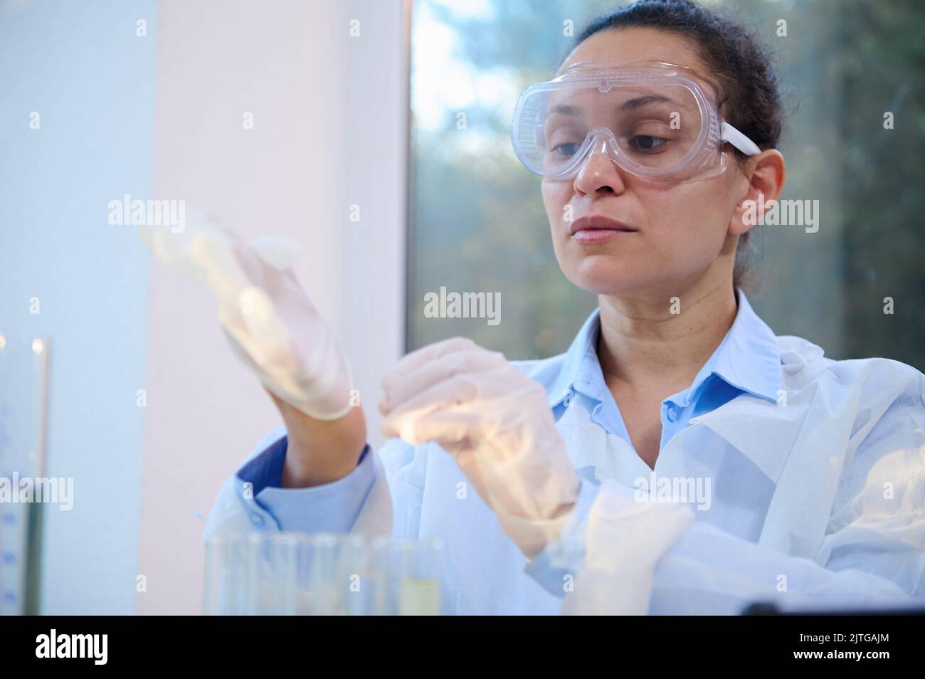 Confident woman scientist in safety eyewear and lab coat putting on ...