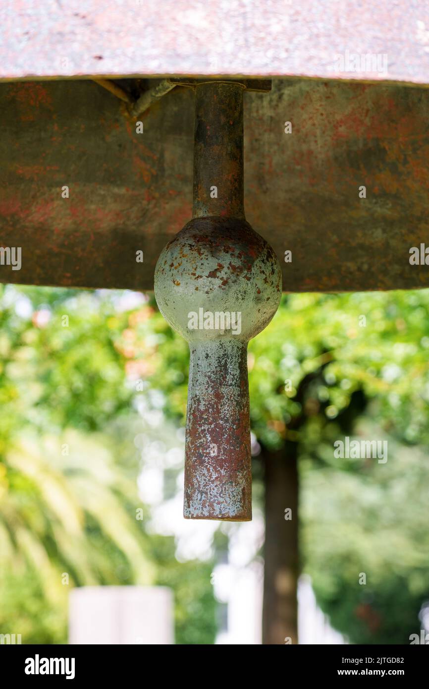 Heavy antique bell clapper against the background of summer foliage of ...