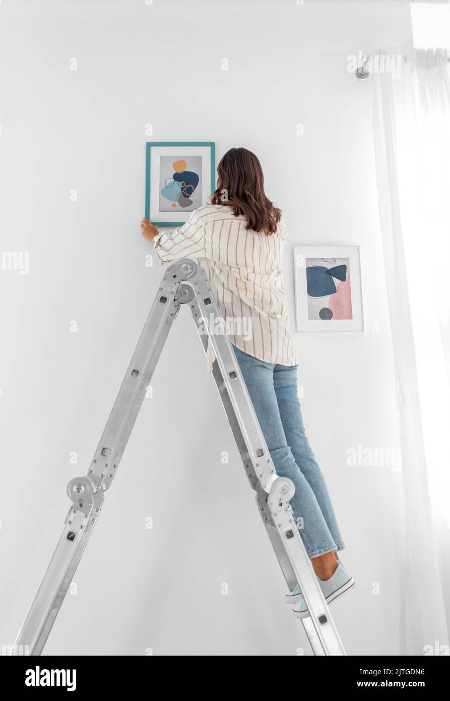 woman on ladder hanging picture in frame on wall Stock Photo - Alamy