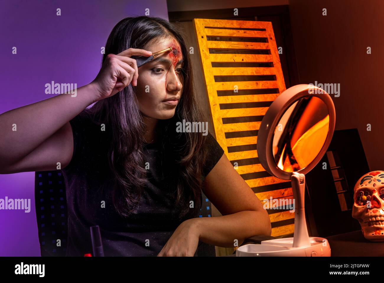 Young woman doing a scary halloween makeup with a wound on her forehead ...