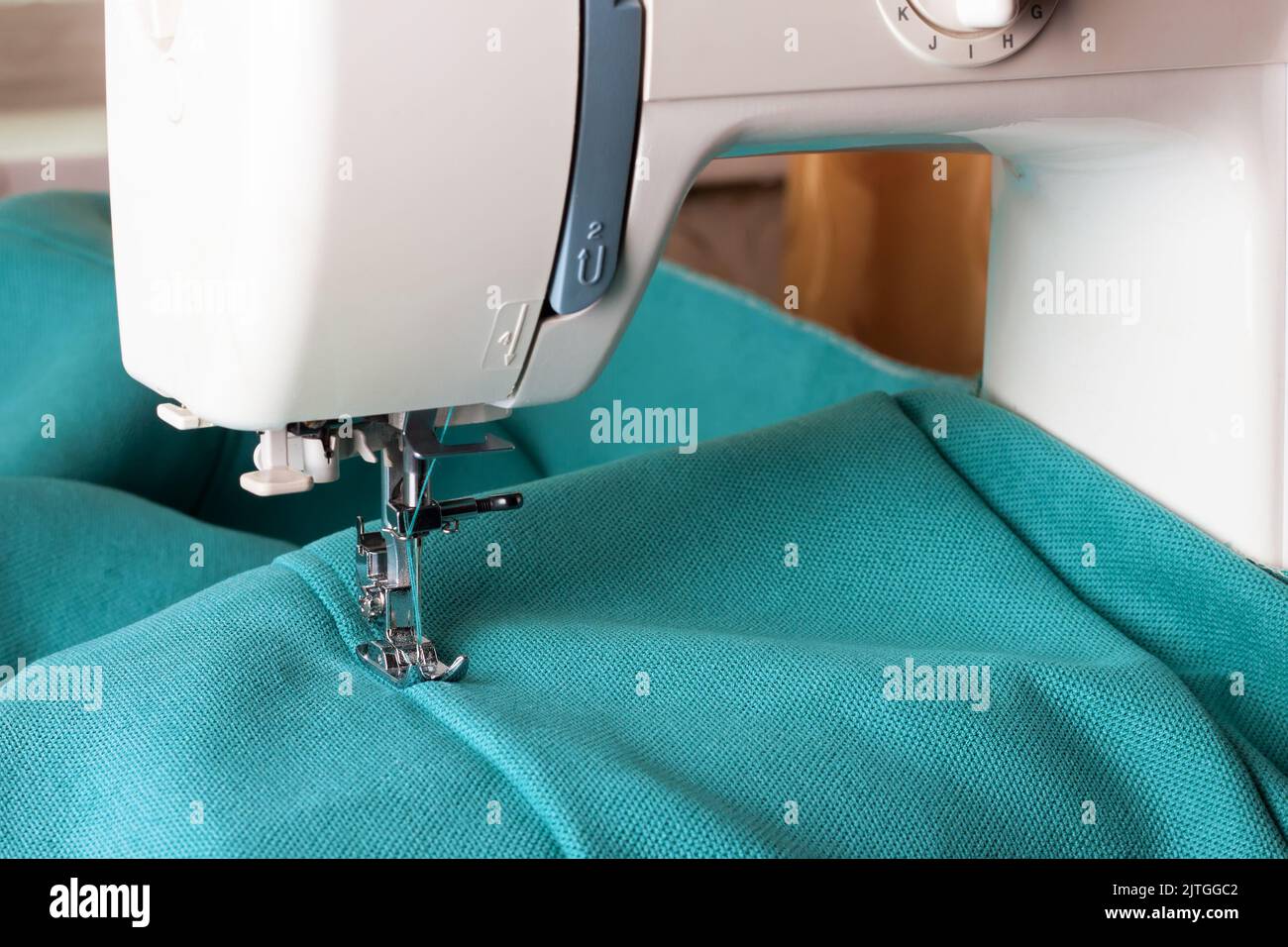 Modern sewing machine working with turquoise fabric. Sewing process ...
