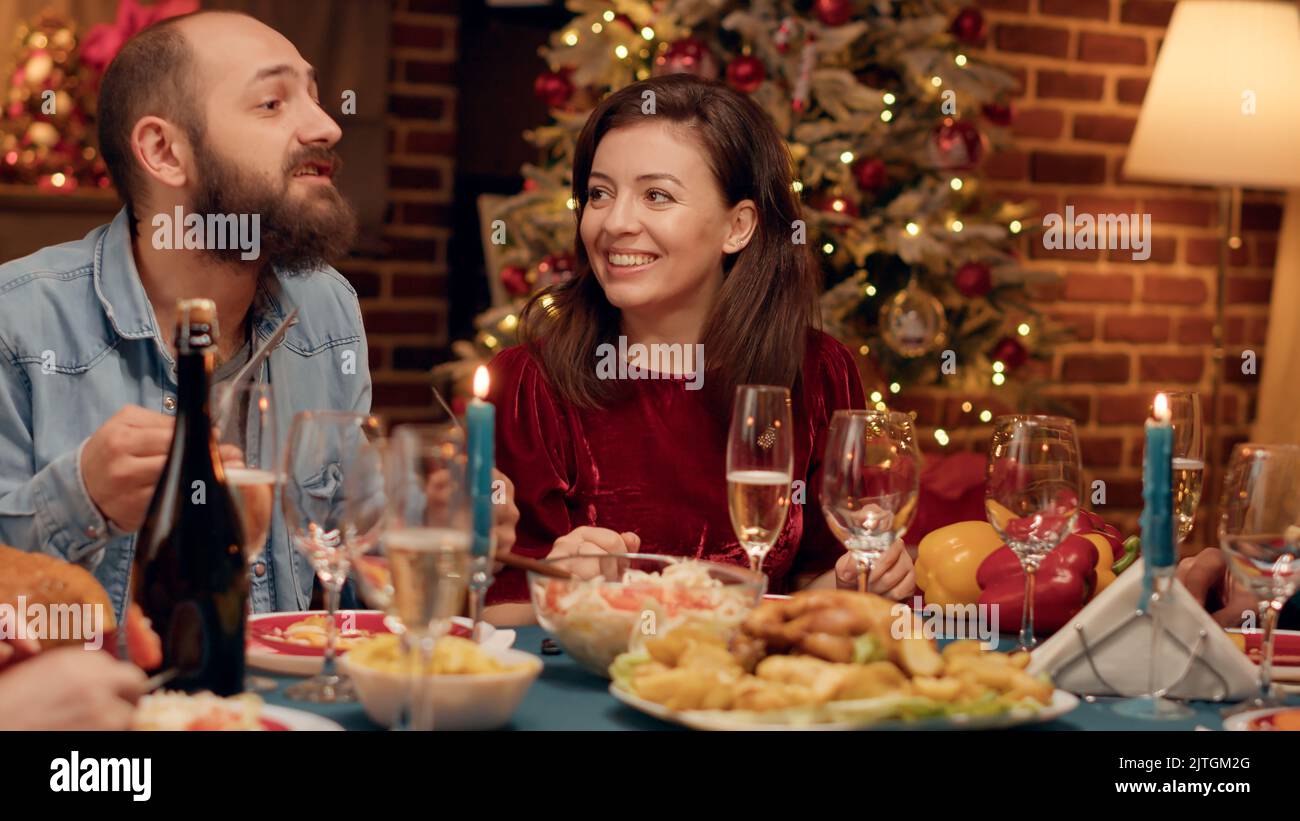 Festive married couple enjoying chatting with relatives while sitting at Christmas dinner table ...