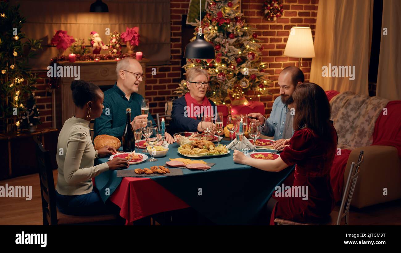 Laughing diverse people gathered around Christmas dinner table clinking ...