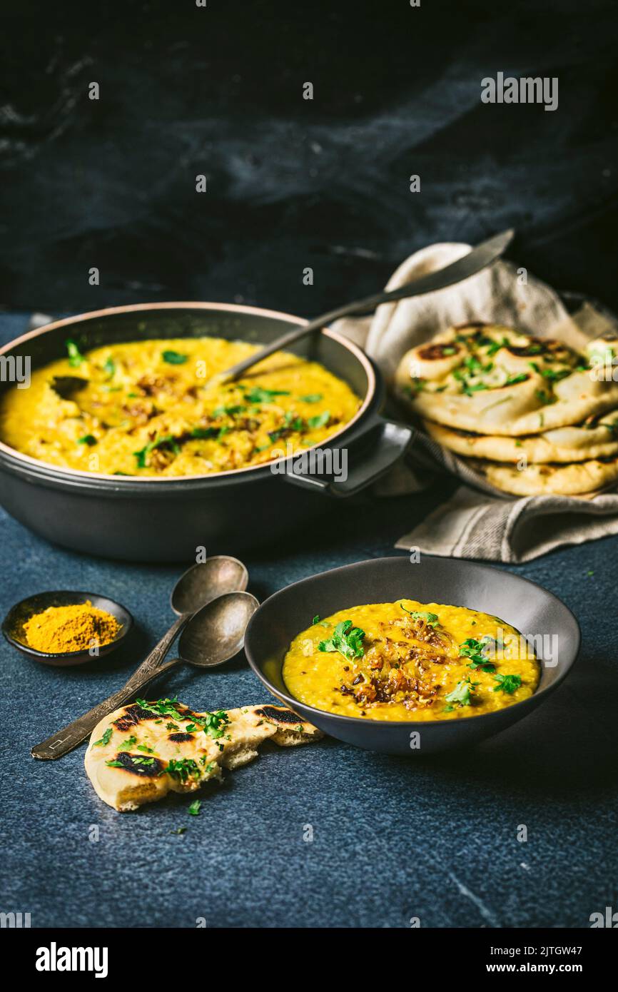 Curried yellow lentils in a large bowl and a serving bowl with naan ...