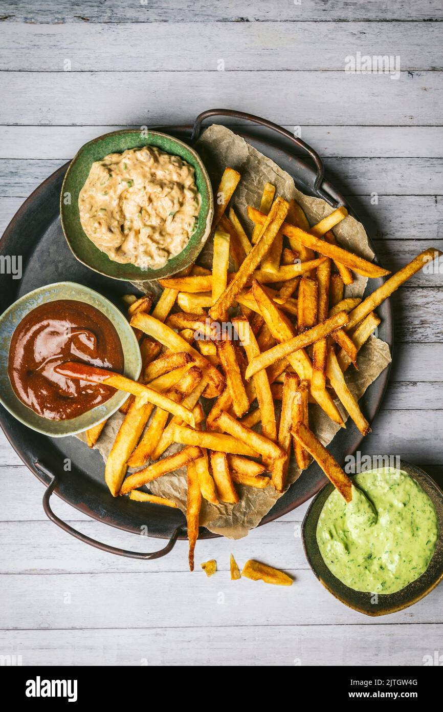 Pommes frites (chips, fries) on parchment and platter with three dips ...