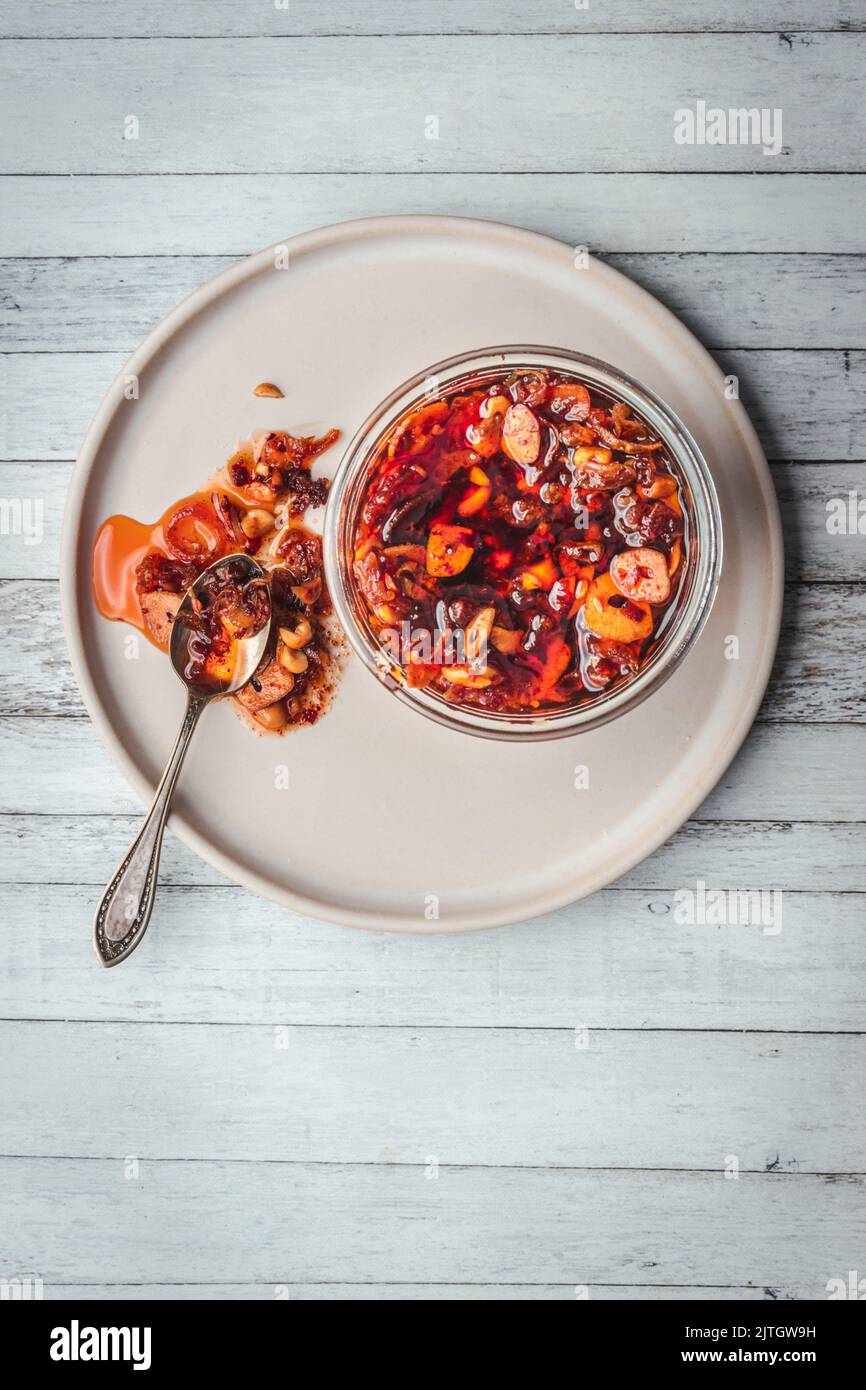 Spicy Asian chili in oil in a jar with spoon and artful spill on the ...