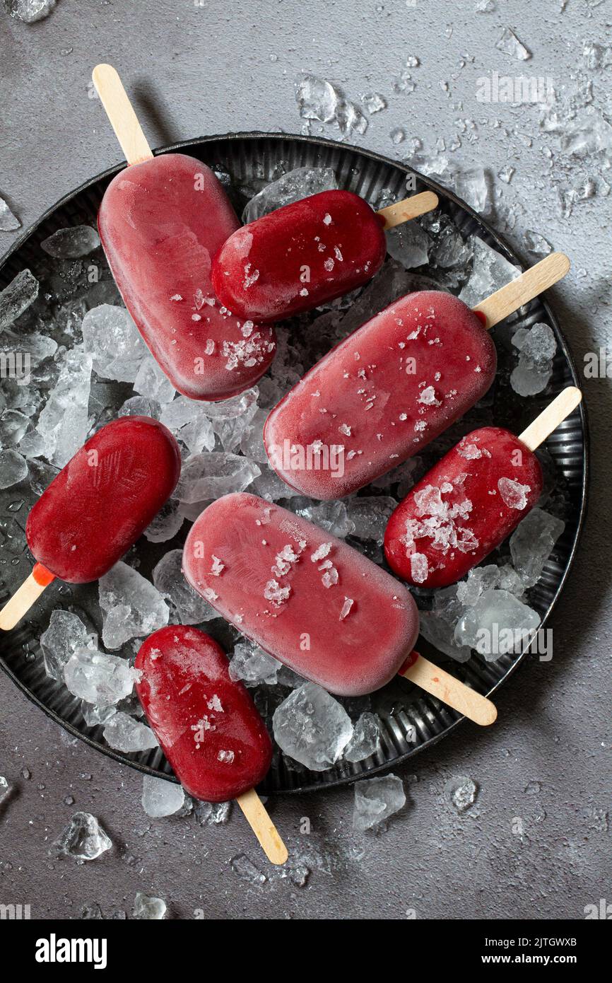 A plate of small and full-sized cherry popsicles (ice lollies) with ...