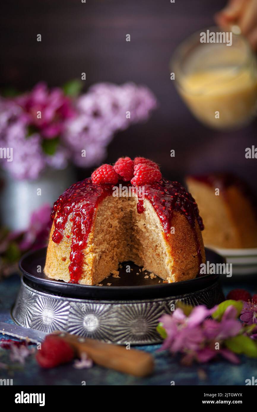 A steamed sponge pudding topped with raspberry jam with a slice removed ...