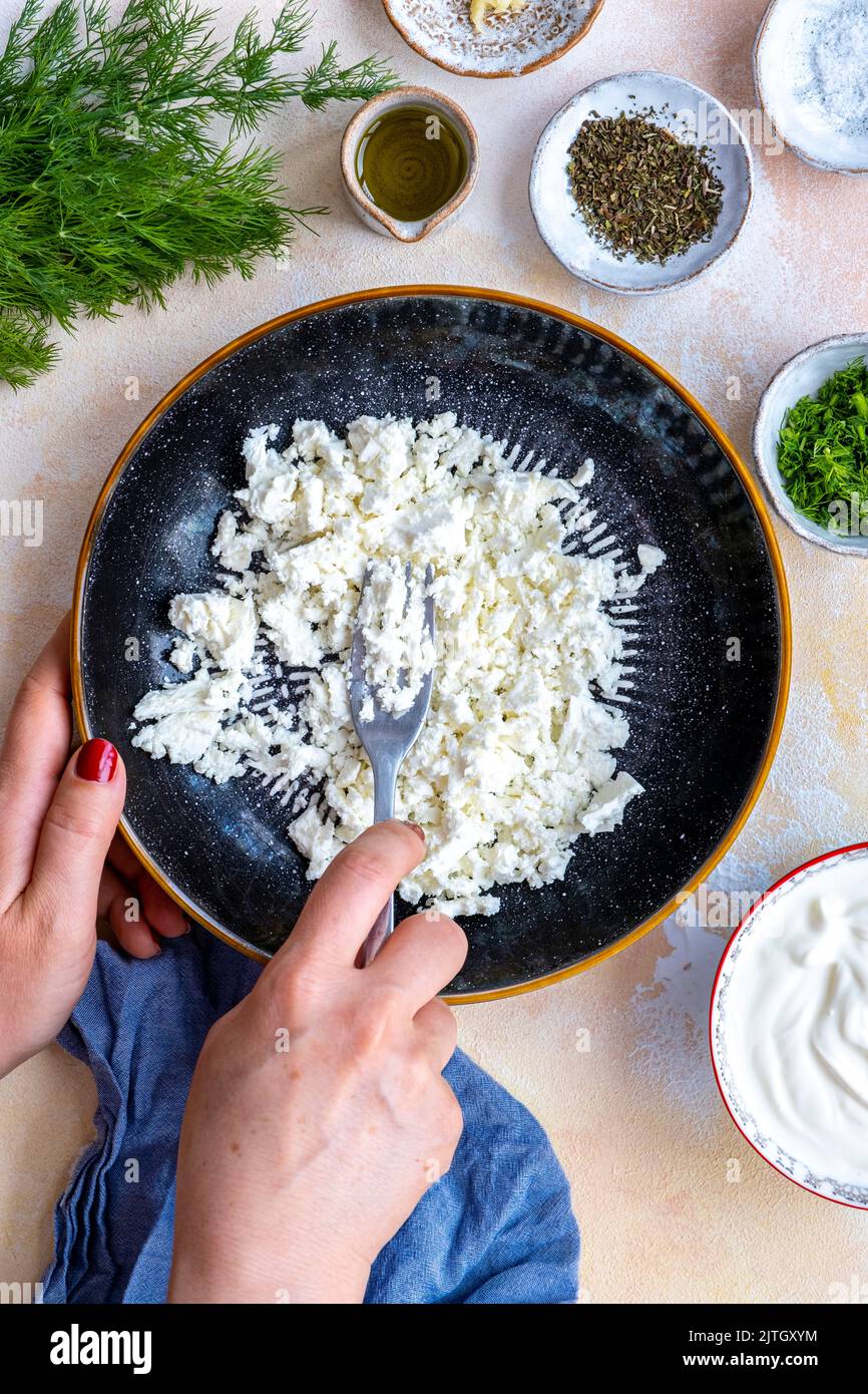 Woman hands crumbling feta cheese using a fork in a black bowl and ...