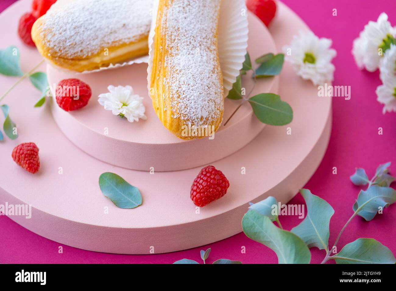 Eclairs cakes.Eclair cakes and raspberries on a pink podium on a ...