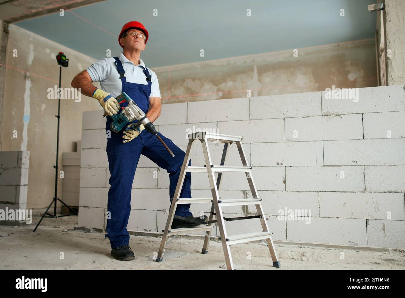 Professional construction worker in uniform standing with rotary hammer ...