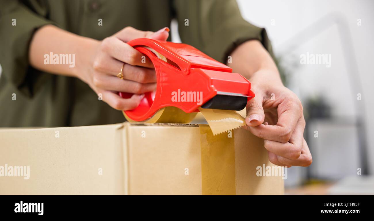 Close up woman hand packing shipment box with transparency tape at home ...