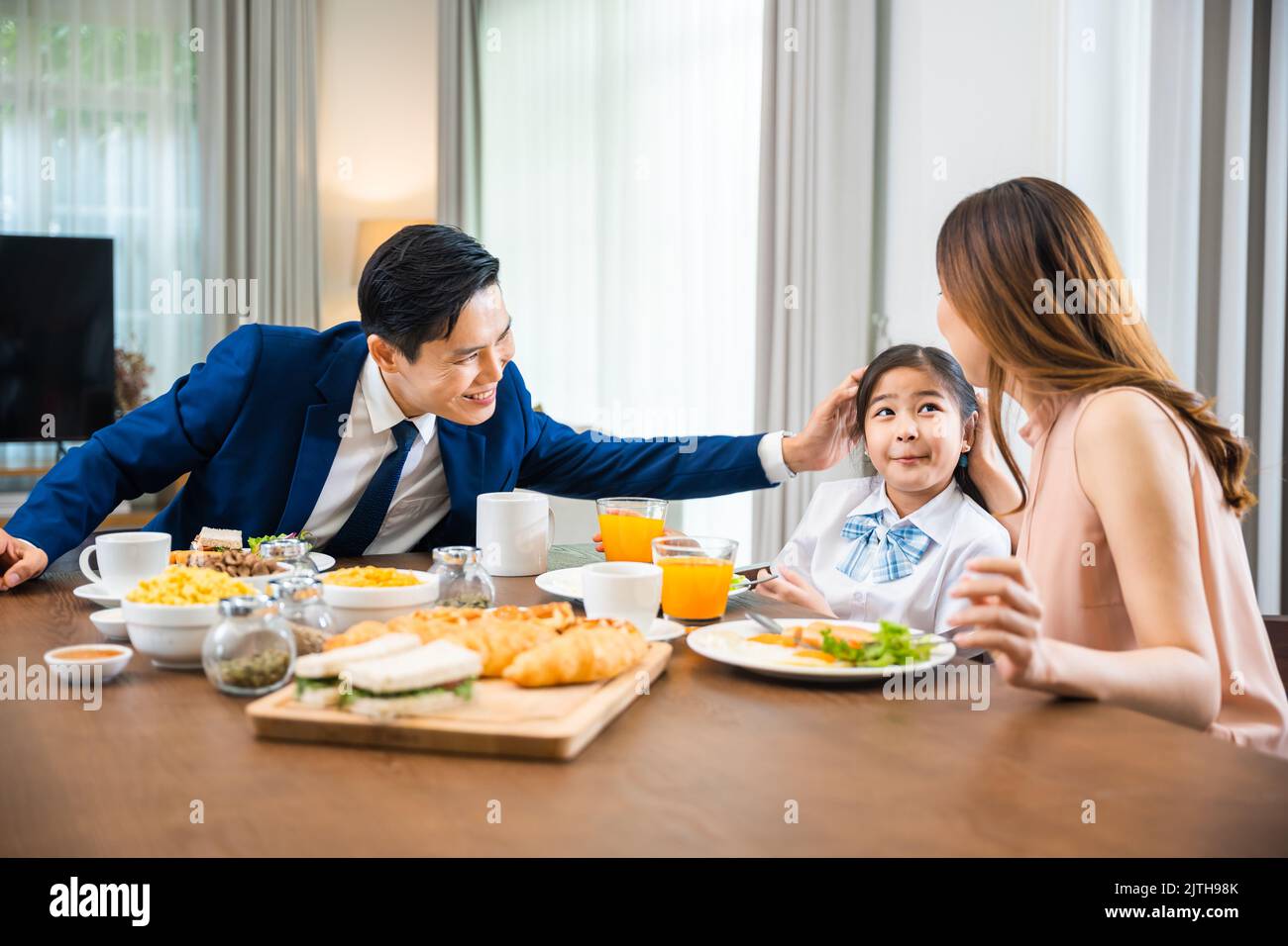 Asian family father, mother with children daughter eating breakfast food on dining table kitchen ...