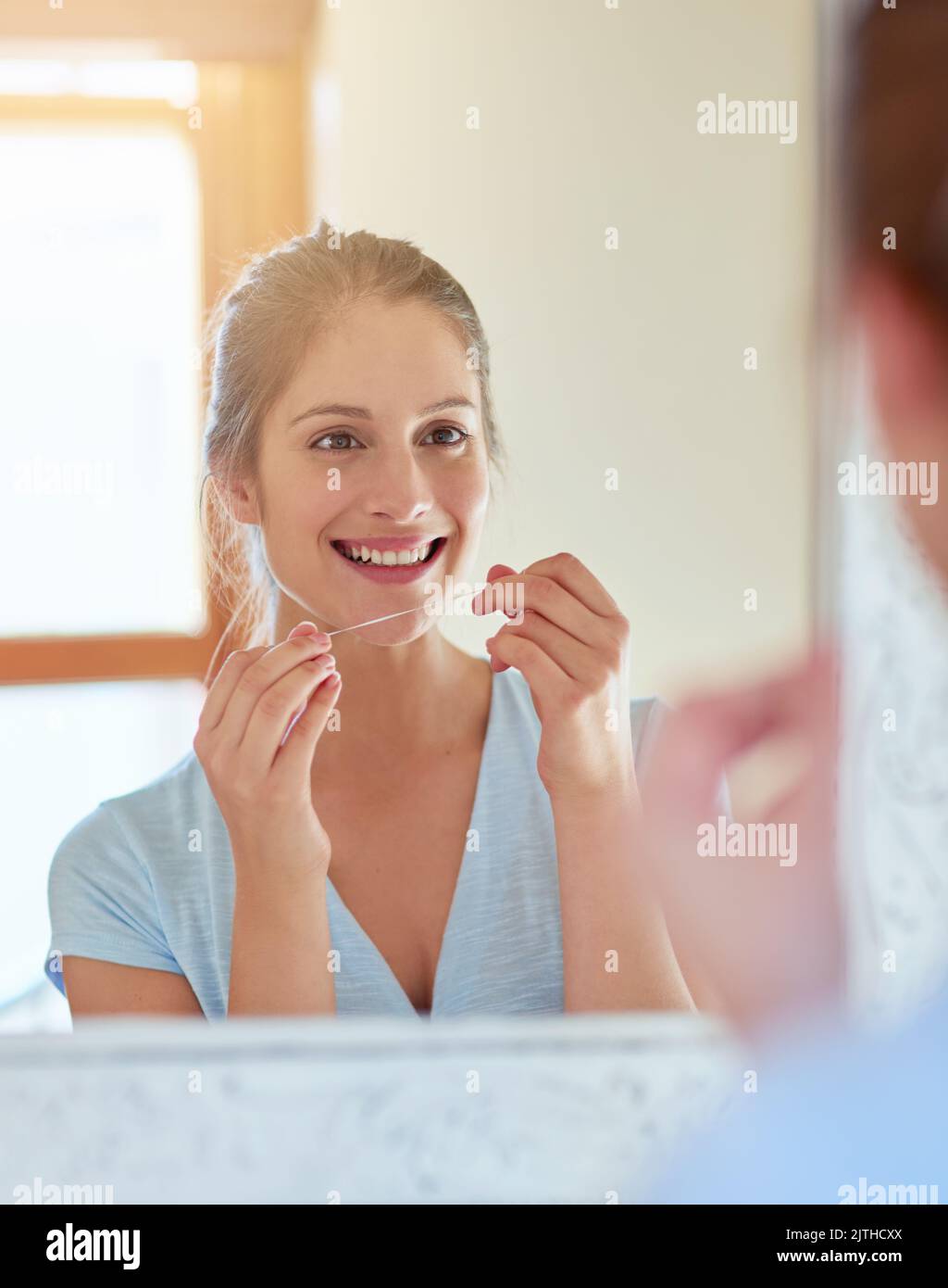 Ensure that you floss every day. a young woman flossing her teeth in a ...