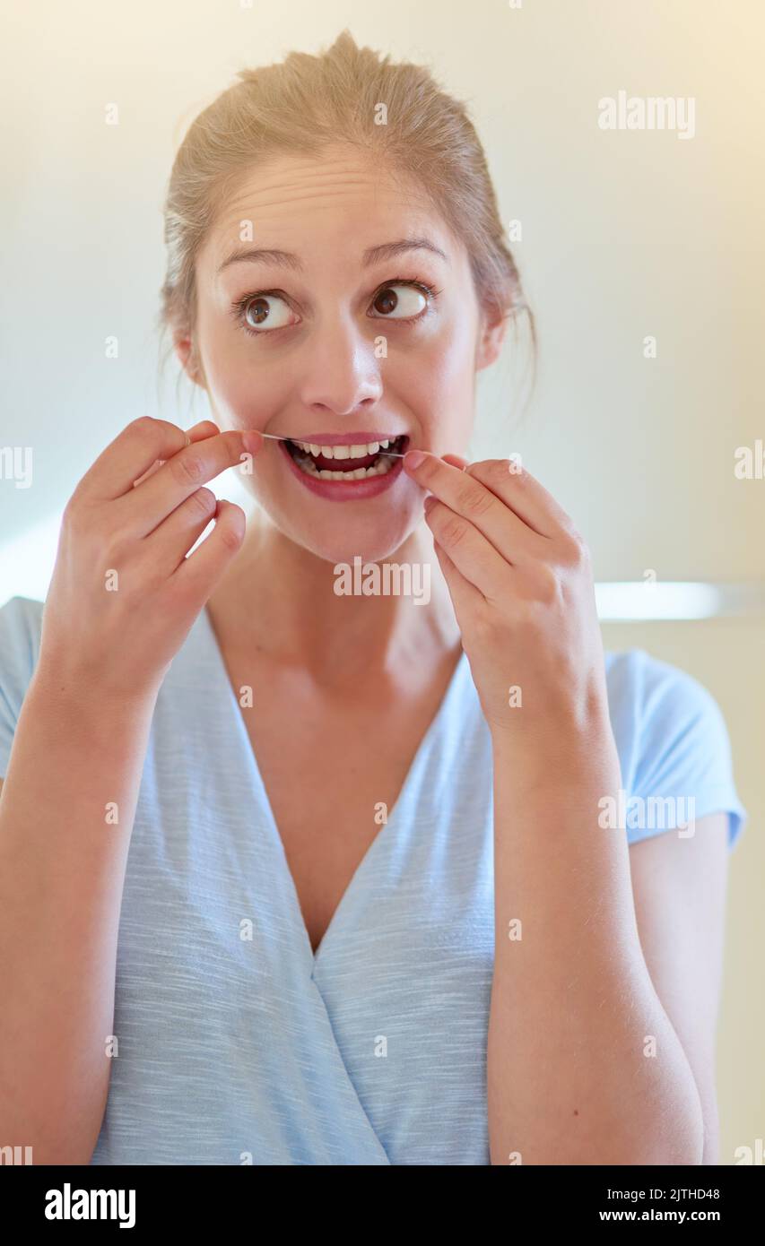 Maintaining good dental hygiene. a young woman flossing her teeth in a ...