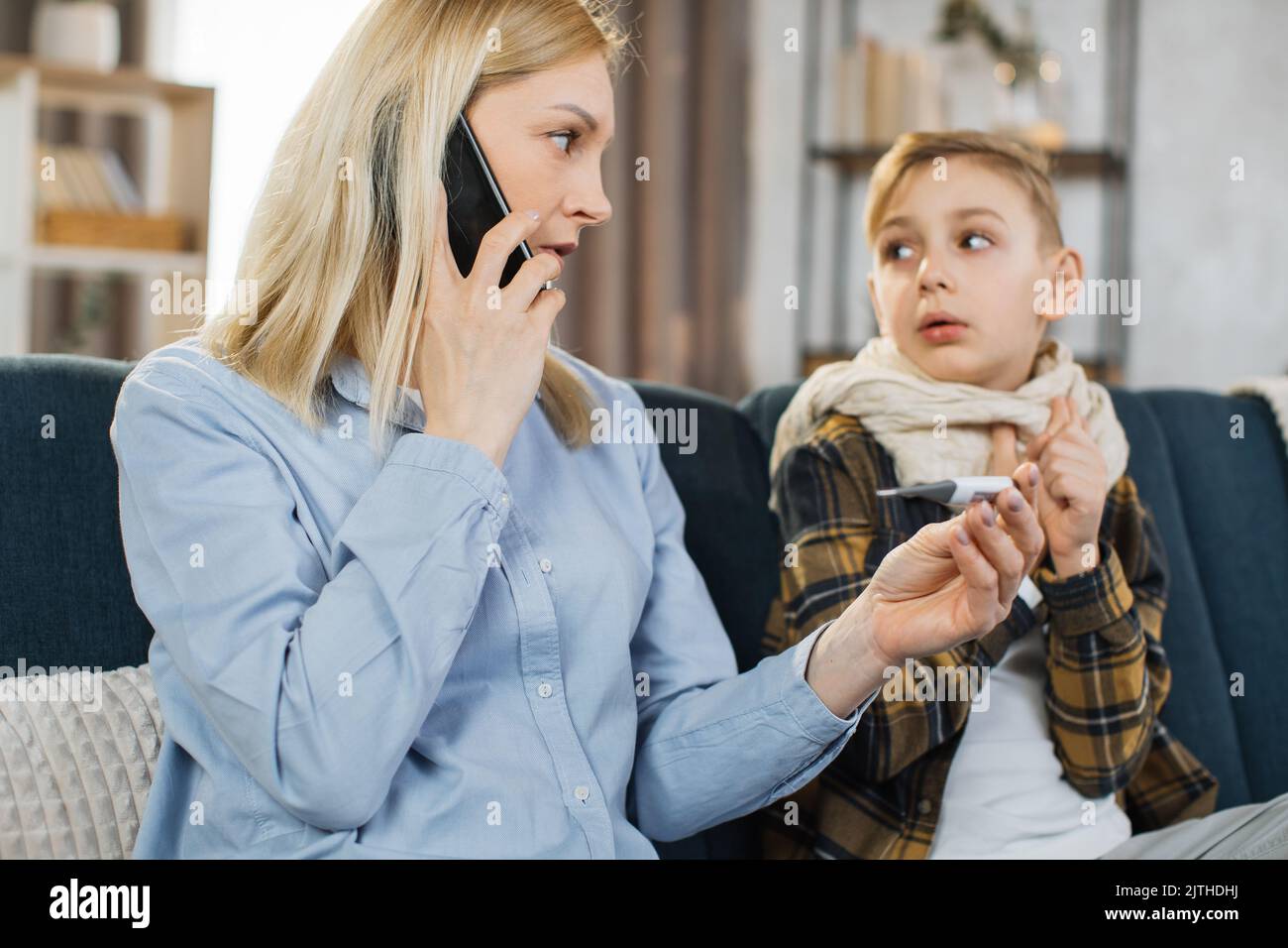Sad sick teen boy with scarf around neck sitting on sofa at home while ...