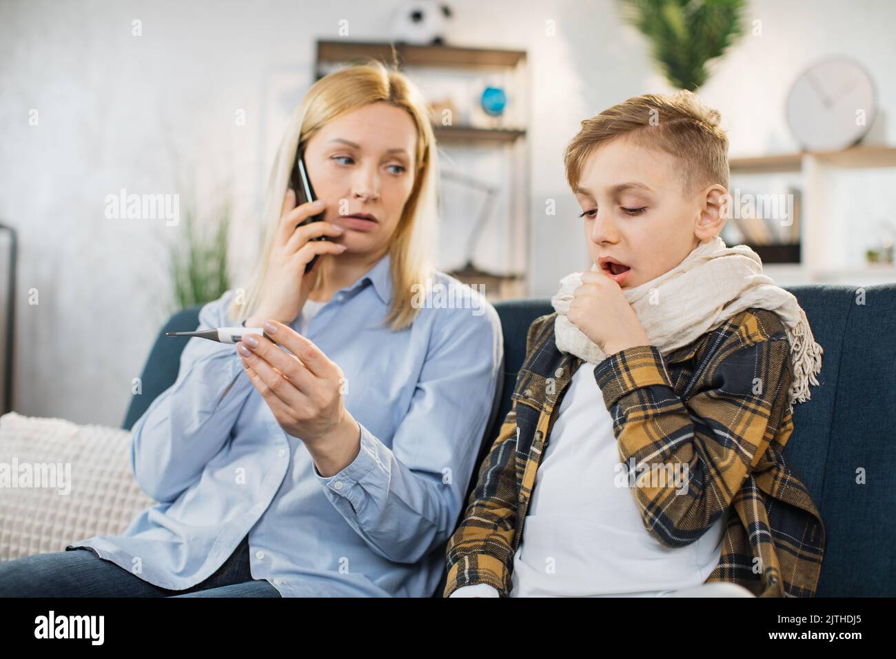 Mother holding thermometer and cell phone, calling to doctor, while ...