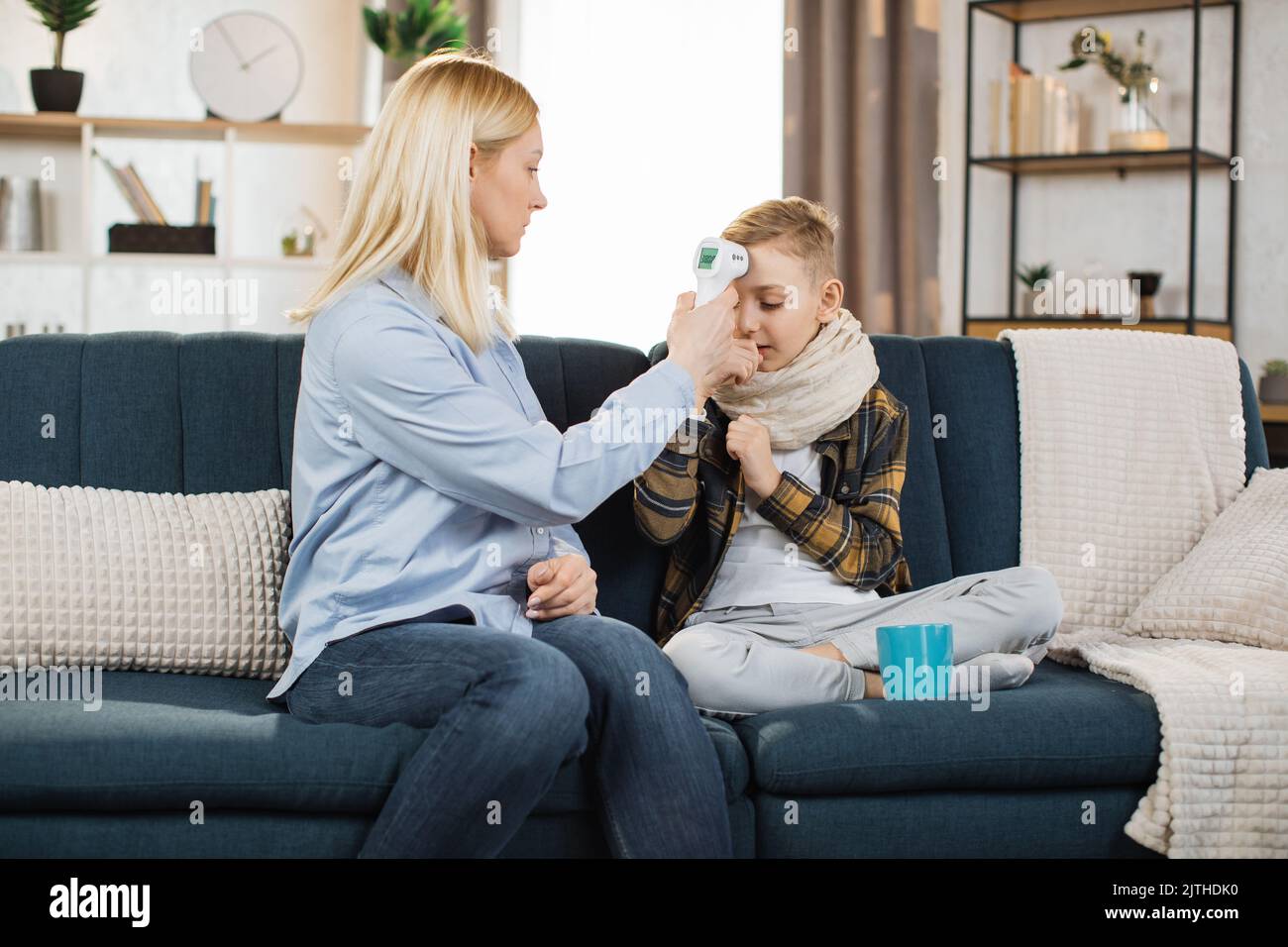 Middle aged worried caring blond woman, mother, sitting on sofa at home ...