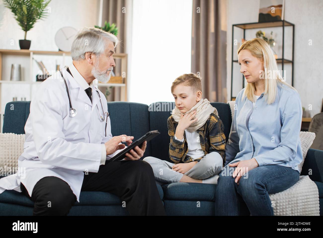 Mature doctor visits little sick boy patient with his mother at home ...