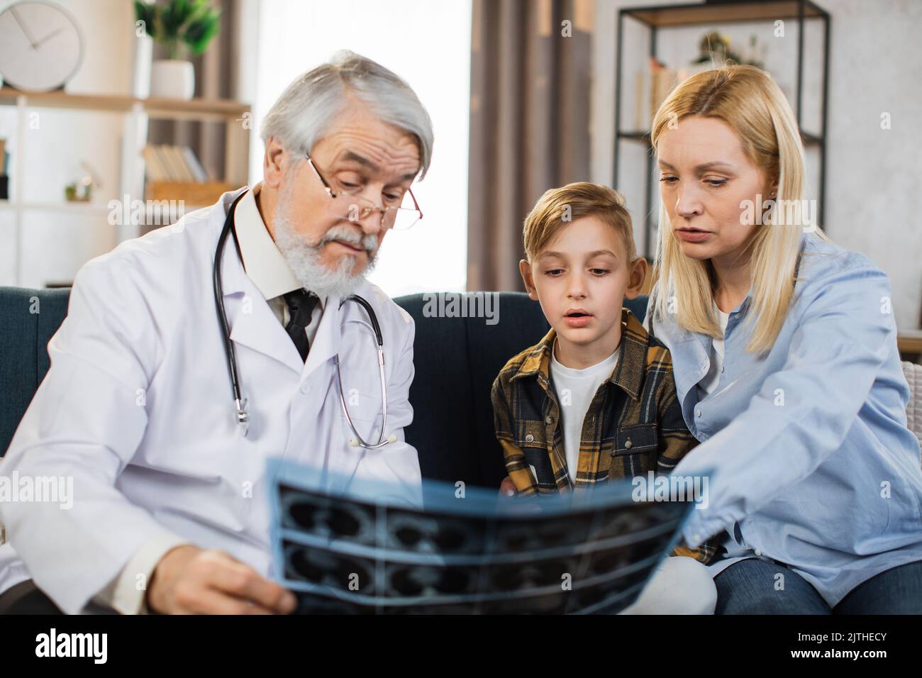 Senior male doctor, sick little boy and his mom looking at x-ray scan ...
