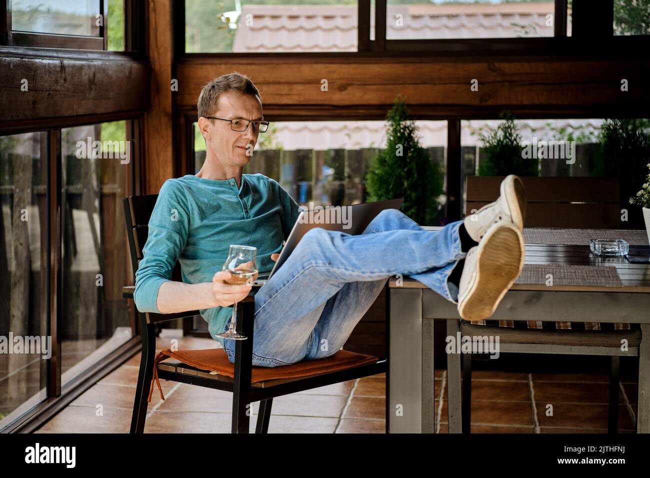 Middle aged man wearing glasses using laptop, sitting in cozy armchair ...