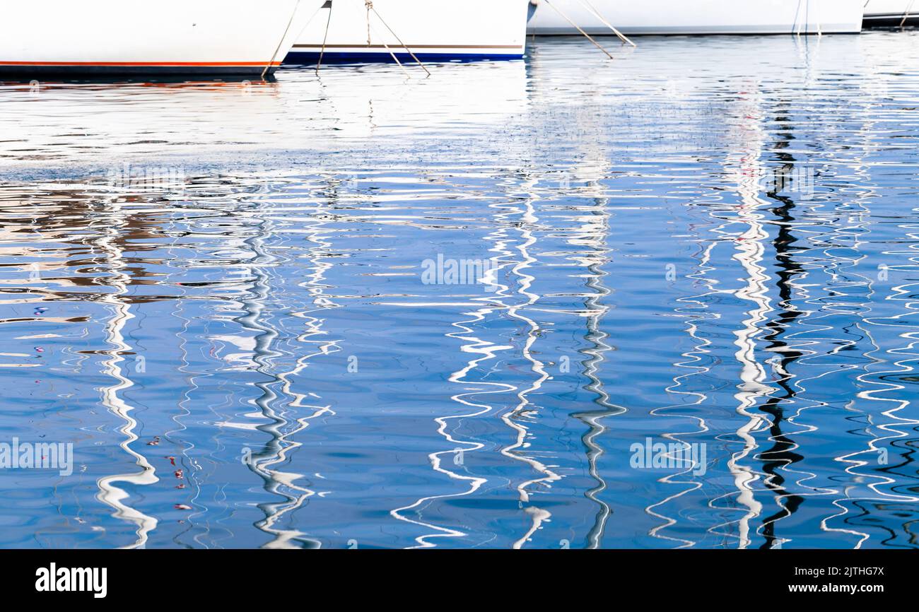 Rippled sea water with reflections of yachts moored in marina on a ...
