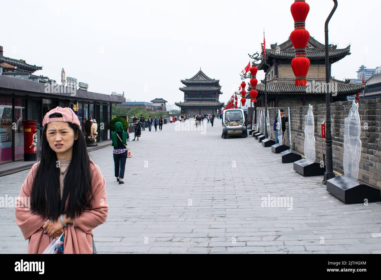 A young Chinese woman and more tourists walking on the Xi'an City Wall ...