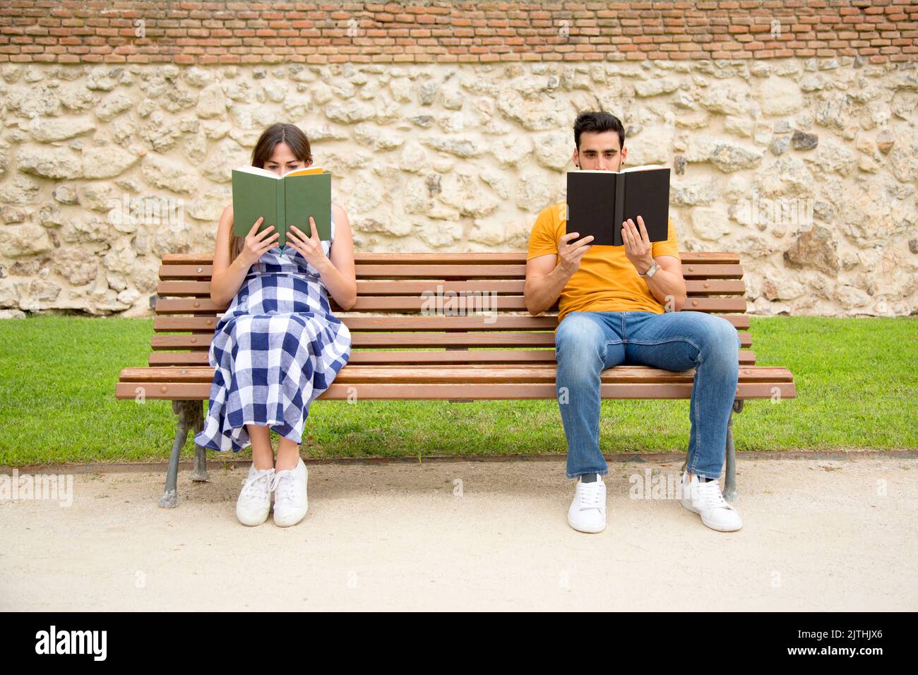 Frontal view of two people sitting on a bench of a park reading books ...
