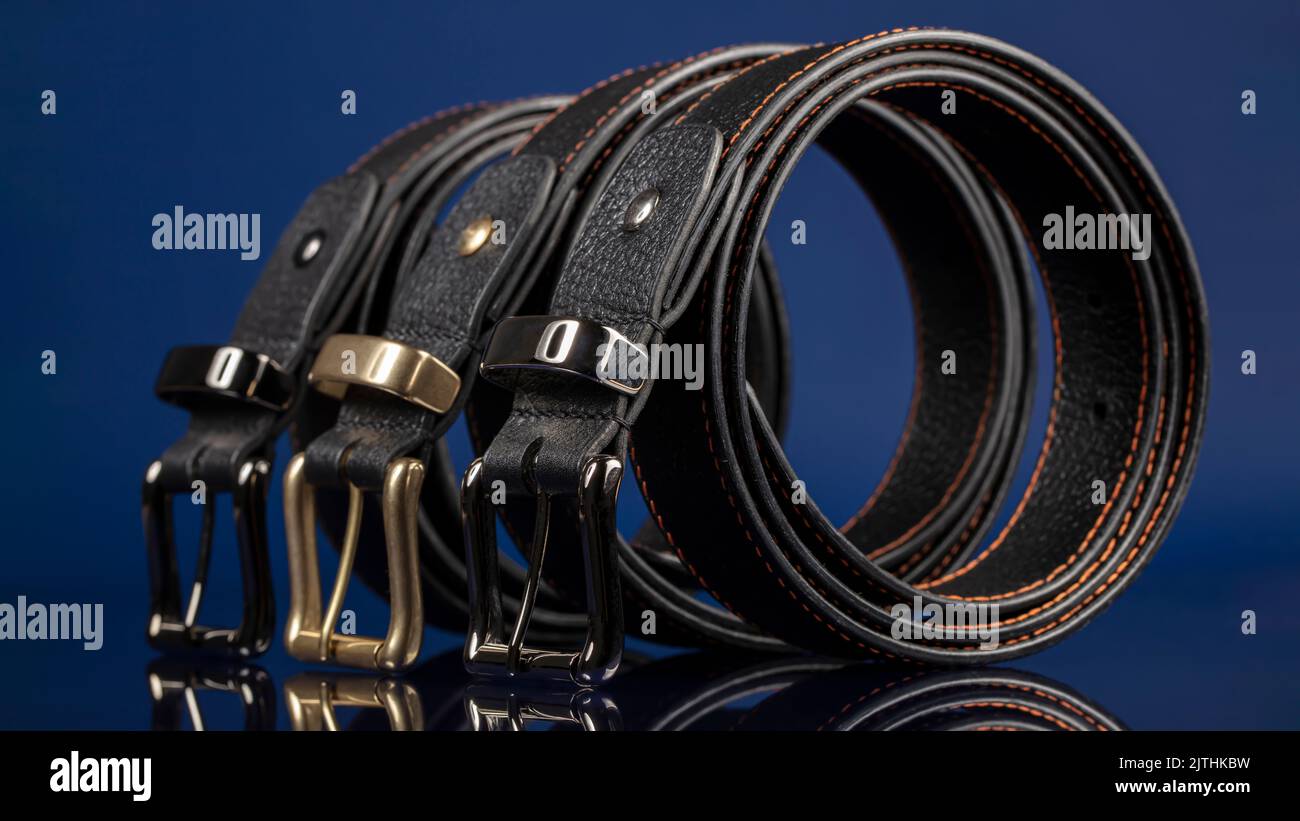 Group of black leather belts on a blue background Stock Photo - Alamy