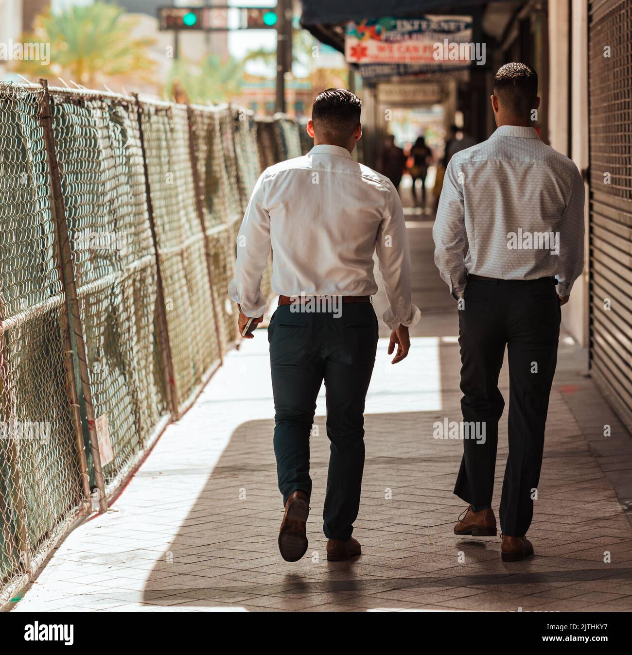 A back view of two men wearing white shirt and walking in footpath ...