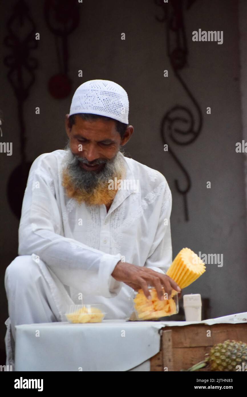 A muslim man peeling off the skin of pineapple to sell in street Stock ...