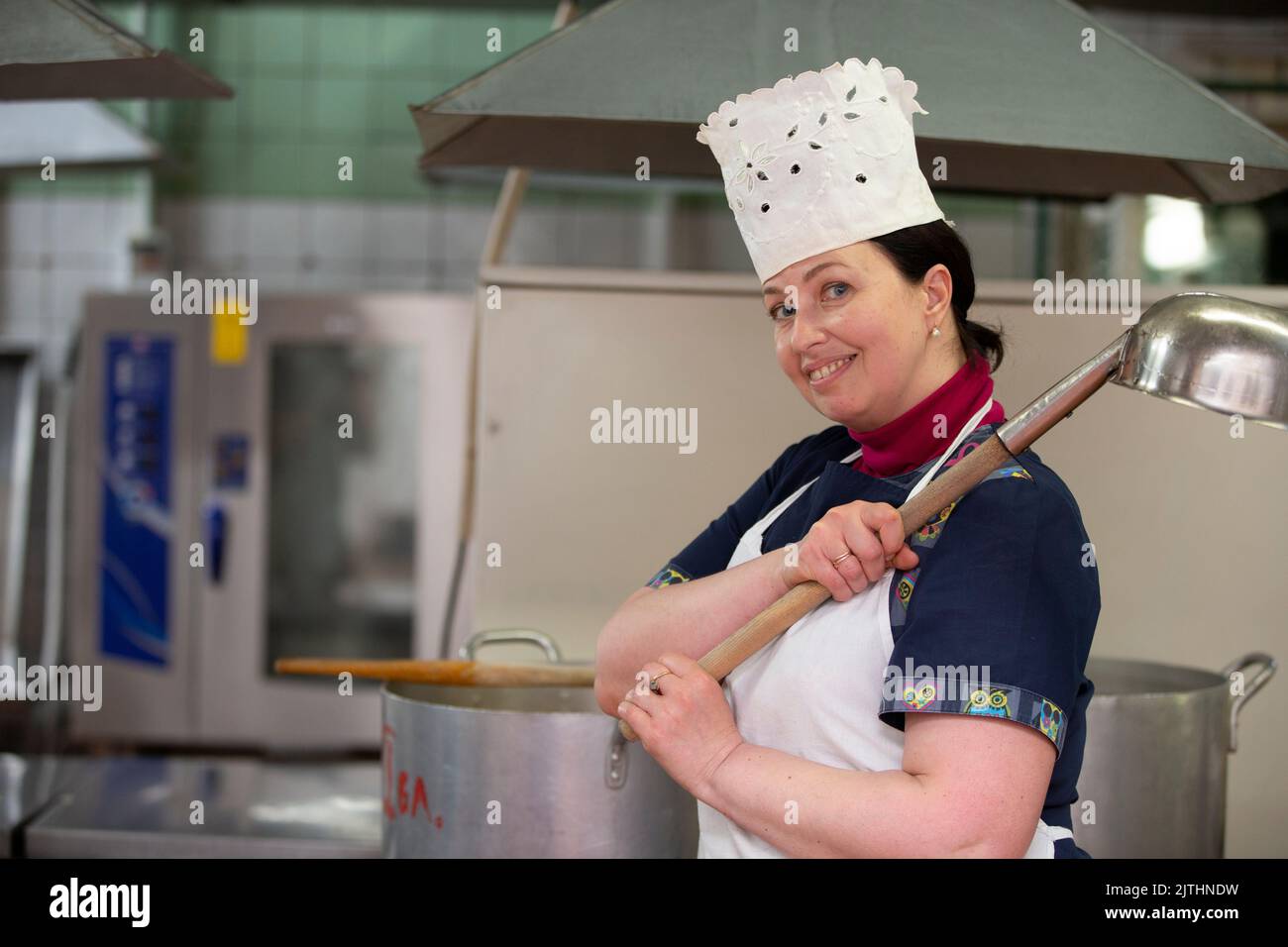 Happy industrial kitchen chef posing with big ladle. Public dining room ...