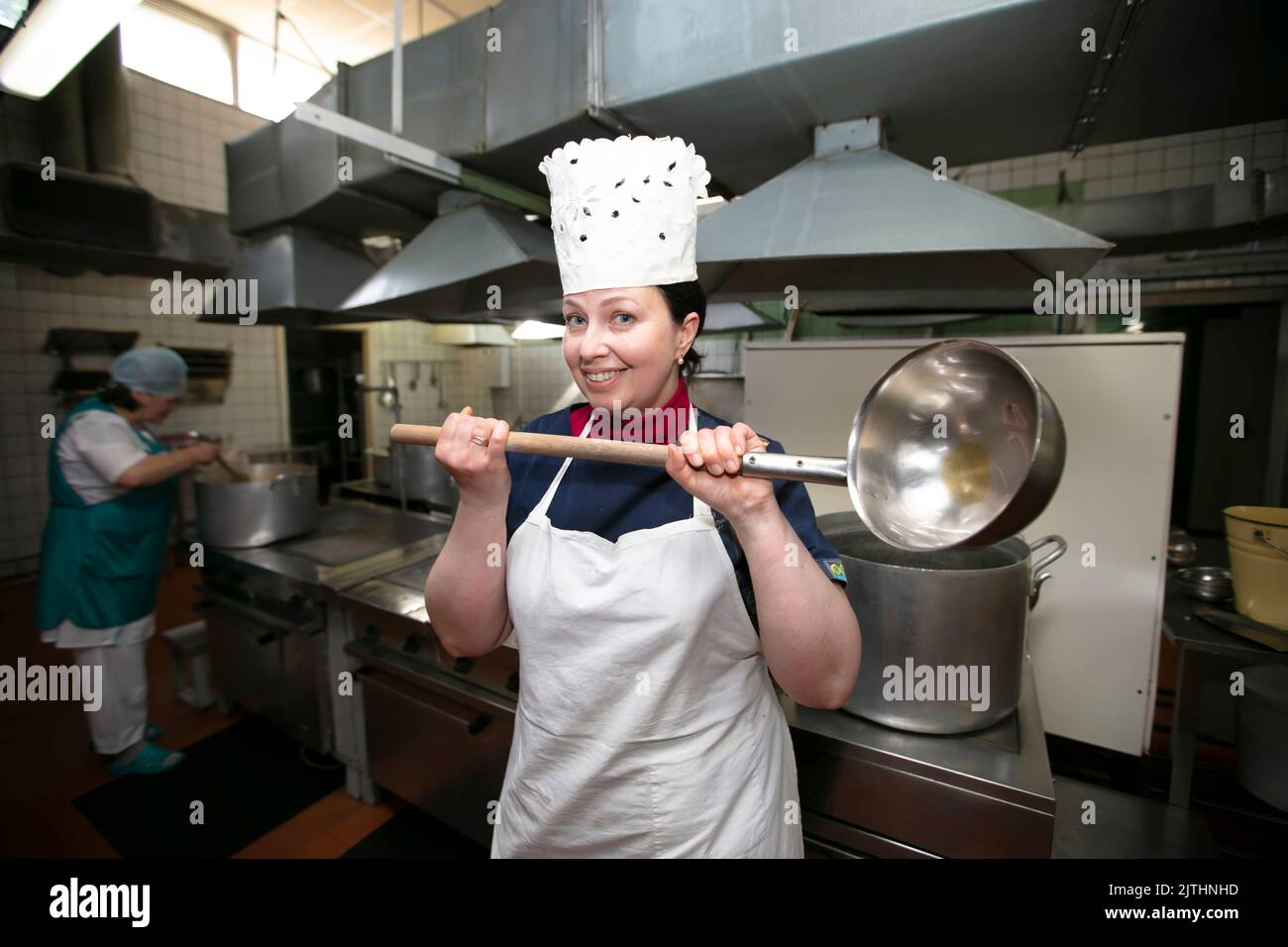 Happy industrial kitchen chef posing with big ladle. Public dining room ...