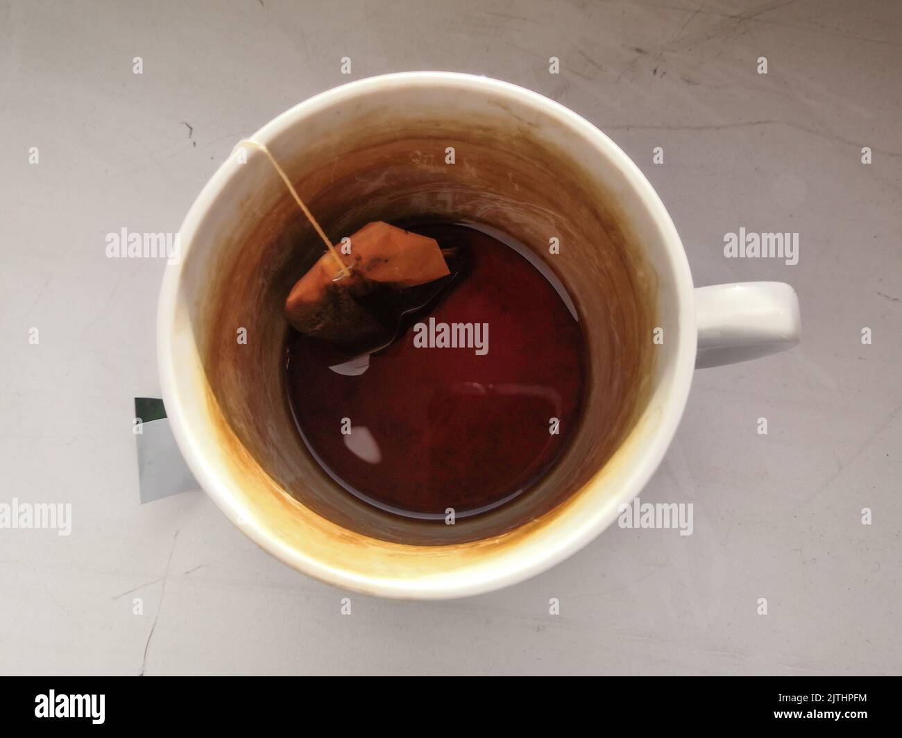 A wet used disposable tea bag lies at the bottom of a dirty ceramic cup ...