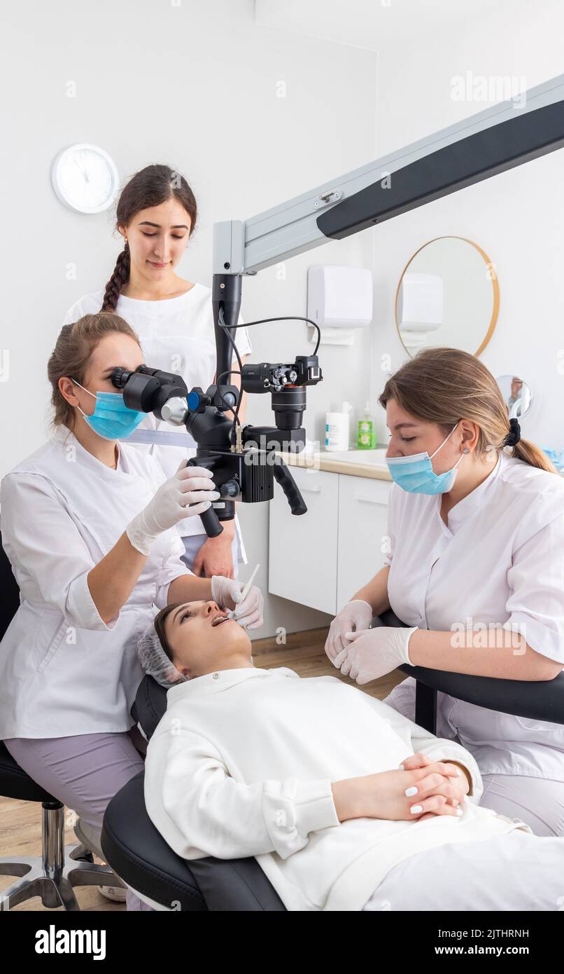 Female dentist using dental microscope treating patient teeth at dental ...