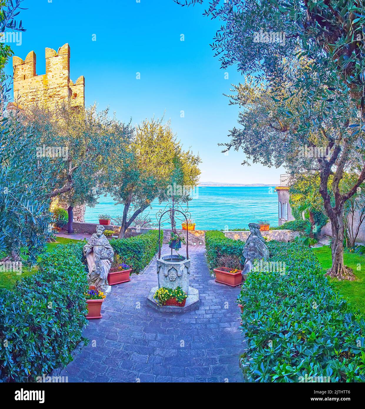 The shady garden with olive trees, green lawn, medieval well and ...