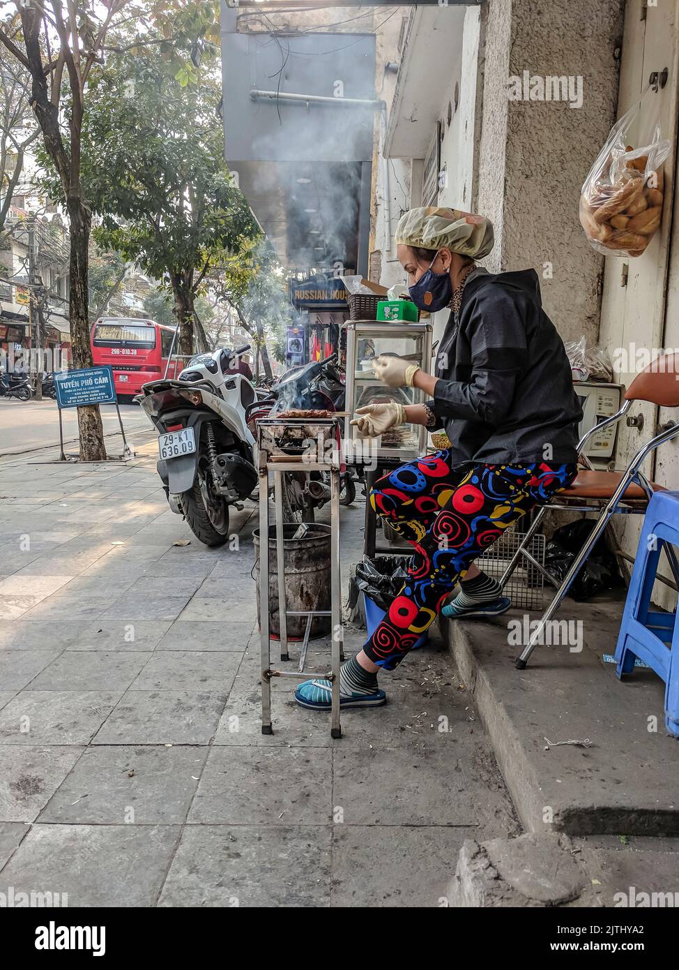 A woman cooks food on the pavement as she prepares to sell street food ...