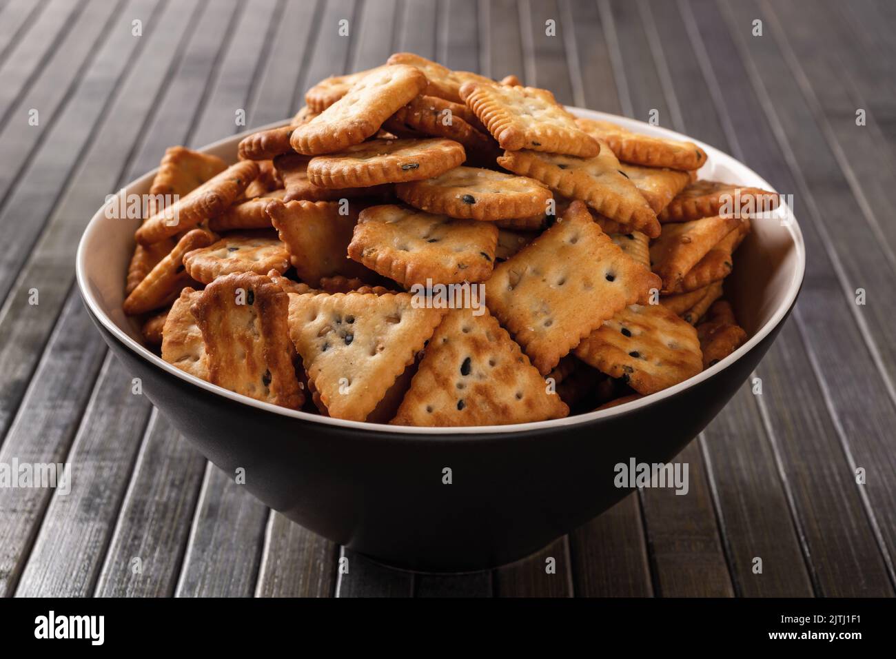 Heap of saltine crackers in a bowl over dark wood plank background ...