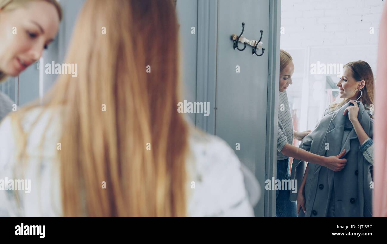 Pretty young woman is checking fashionable coat in fitting room with ...
