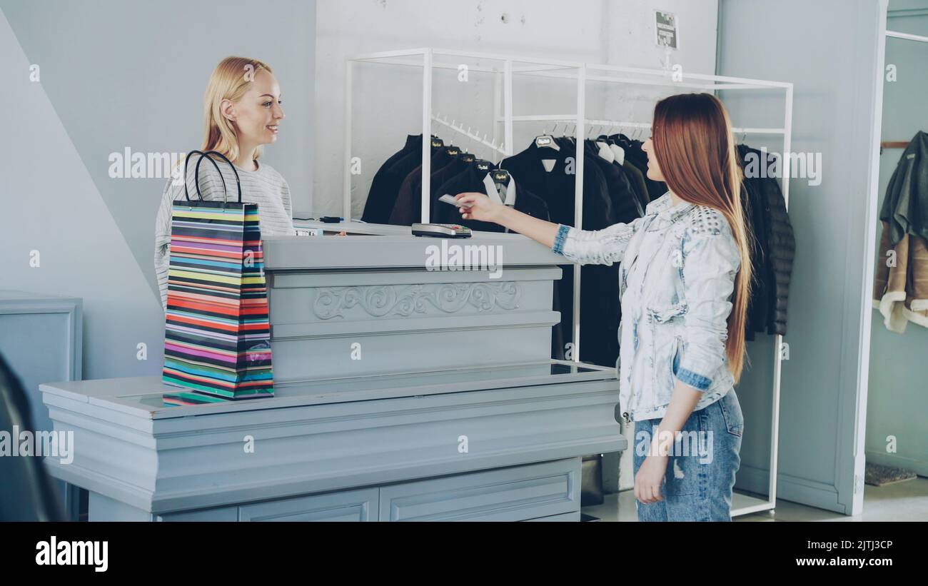 Cheerful customer is paying with credit card for purchased clothes ...