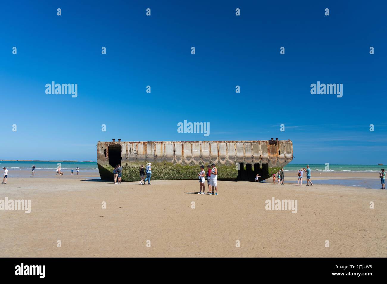 Tourists exploring the remains of the Mulberry harbour on the beach at ...