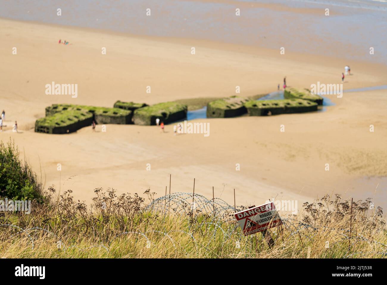 Tourists exploring the remains of the Mulberry harbour on the beach at ...