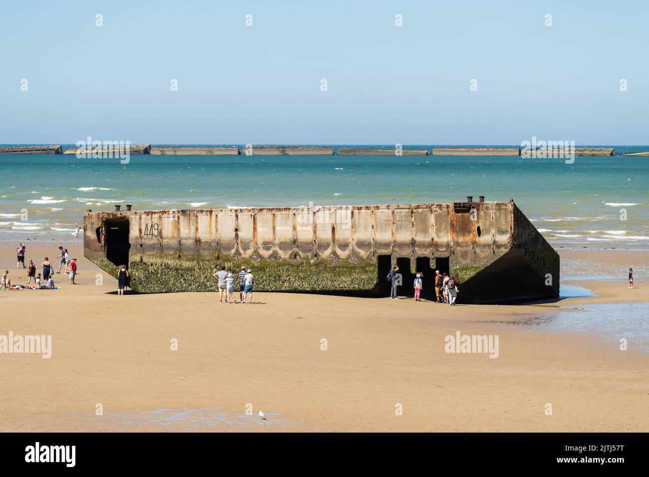 Tourists exploring the remains of the Mulberry harbour on the beach at ...
