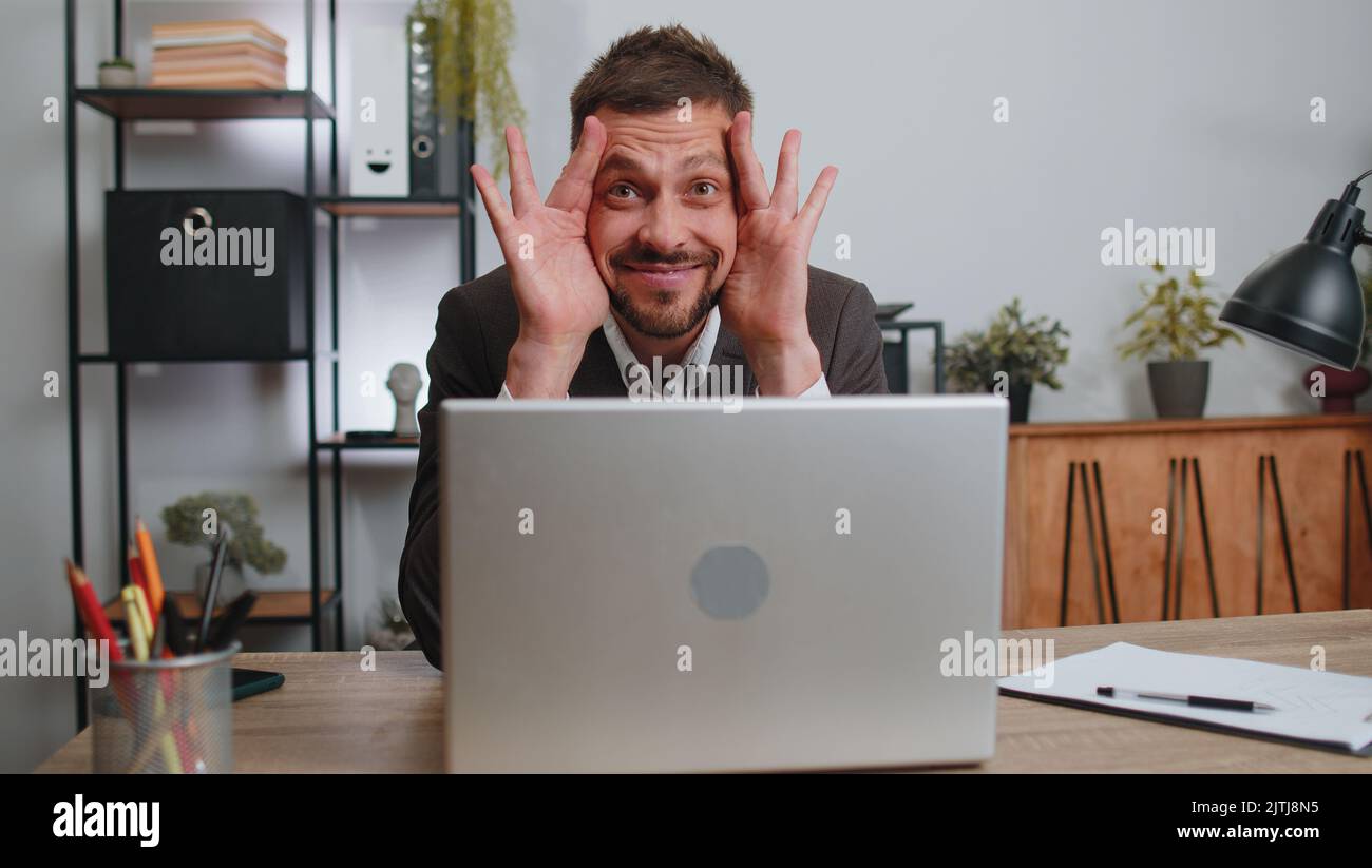 Businessman hiding behind laptop computer, making funny face, fooling ...