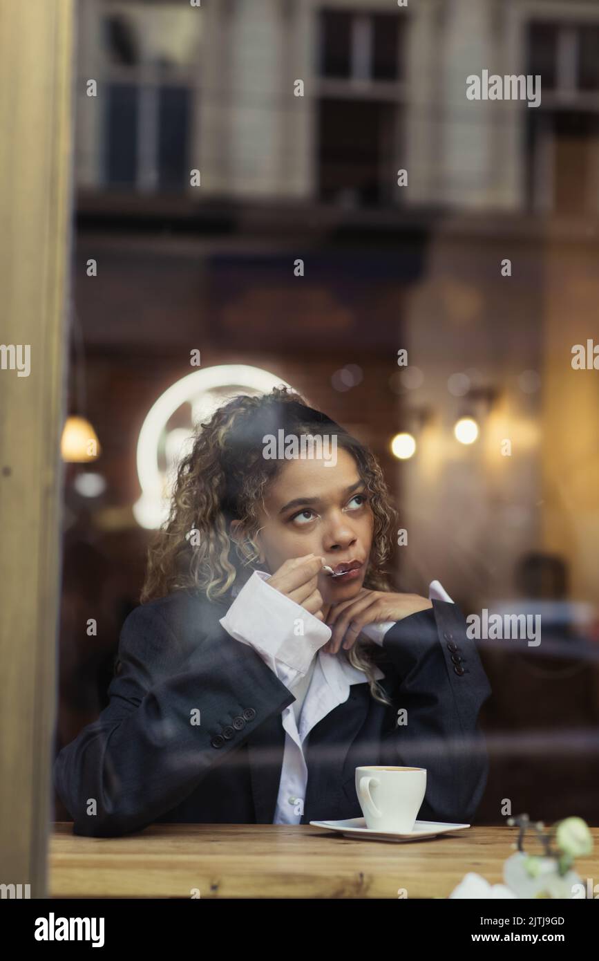 stylish african american woman eating foam from cappuccino cup in cafe ...