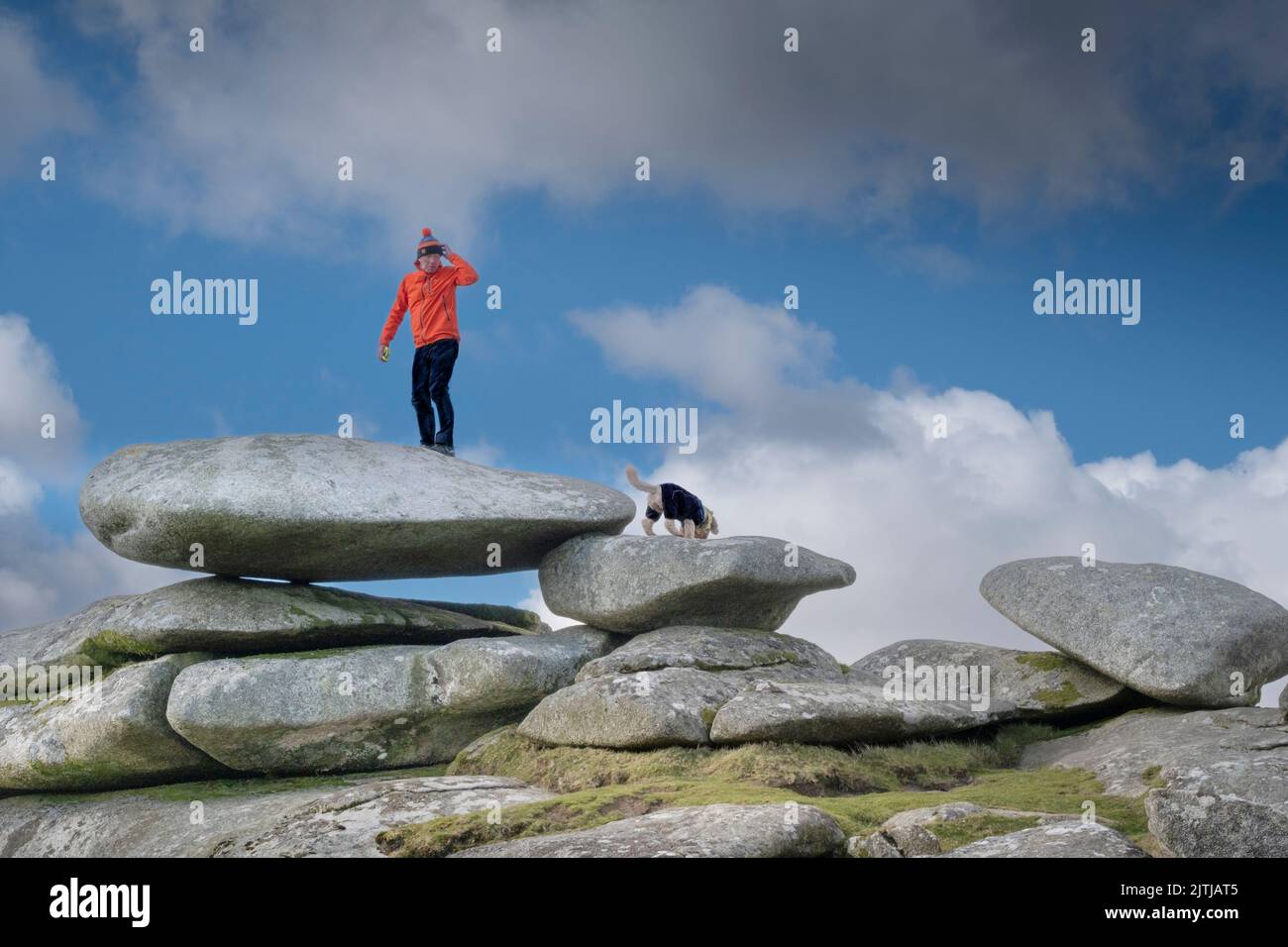 A walker wearing a bright red jacket standing on a huge granite rock ...